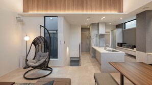 Cozinha moderna com bancada de mármore, forno embutido e pia. Há uma cadeira suspensa e uma mesa com banco na sala de estar.