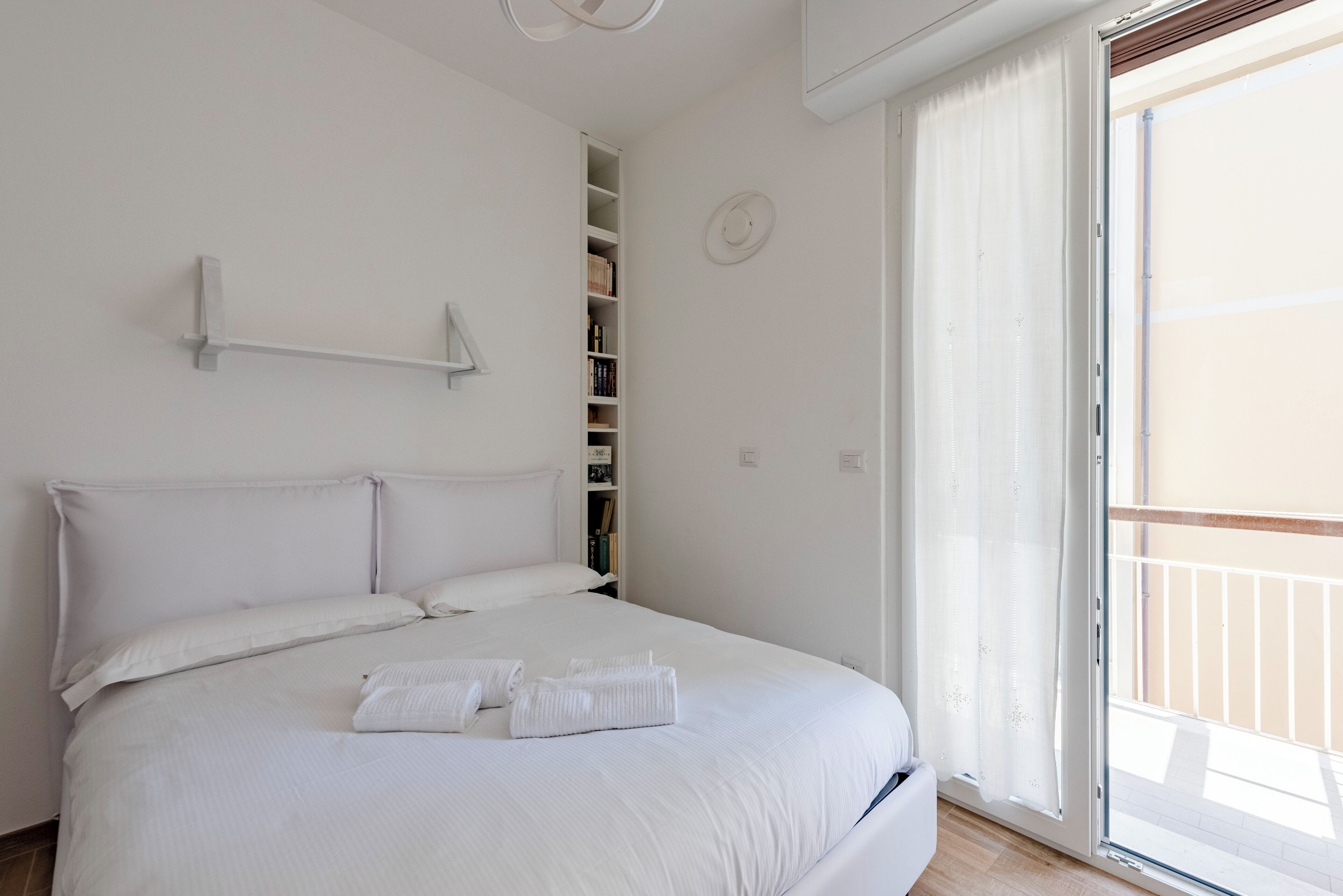 Quarto com cama, guarda-roupa e porta de vidro deslizante para uma varanda.