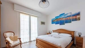 Quarto com cama de madeira, uma cadeira, mesa de cabeceira e parede com três quadros.