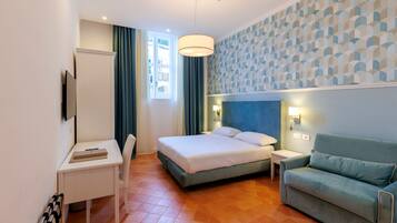 Quarto de hotel com cama, escrivaninha, cadeira, sofá, televisão e janela com cortinas, além de parede com padrão.