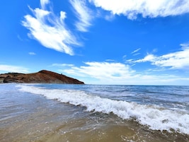 Paisagem costeira com céu limpo e ondas se aproximando da praia.
