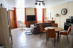 Uma sala de estar moderna com sofá, mesa de jantar, cadeiras, televisão de tela plana e área de cozinha com micro-ondas.