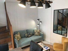 Uma sala de estar com um sofá verde, uma poltrona preta, uma mesa de centro com revistas e uma escada.