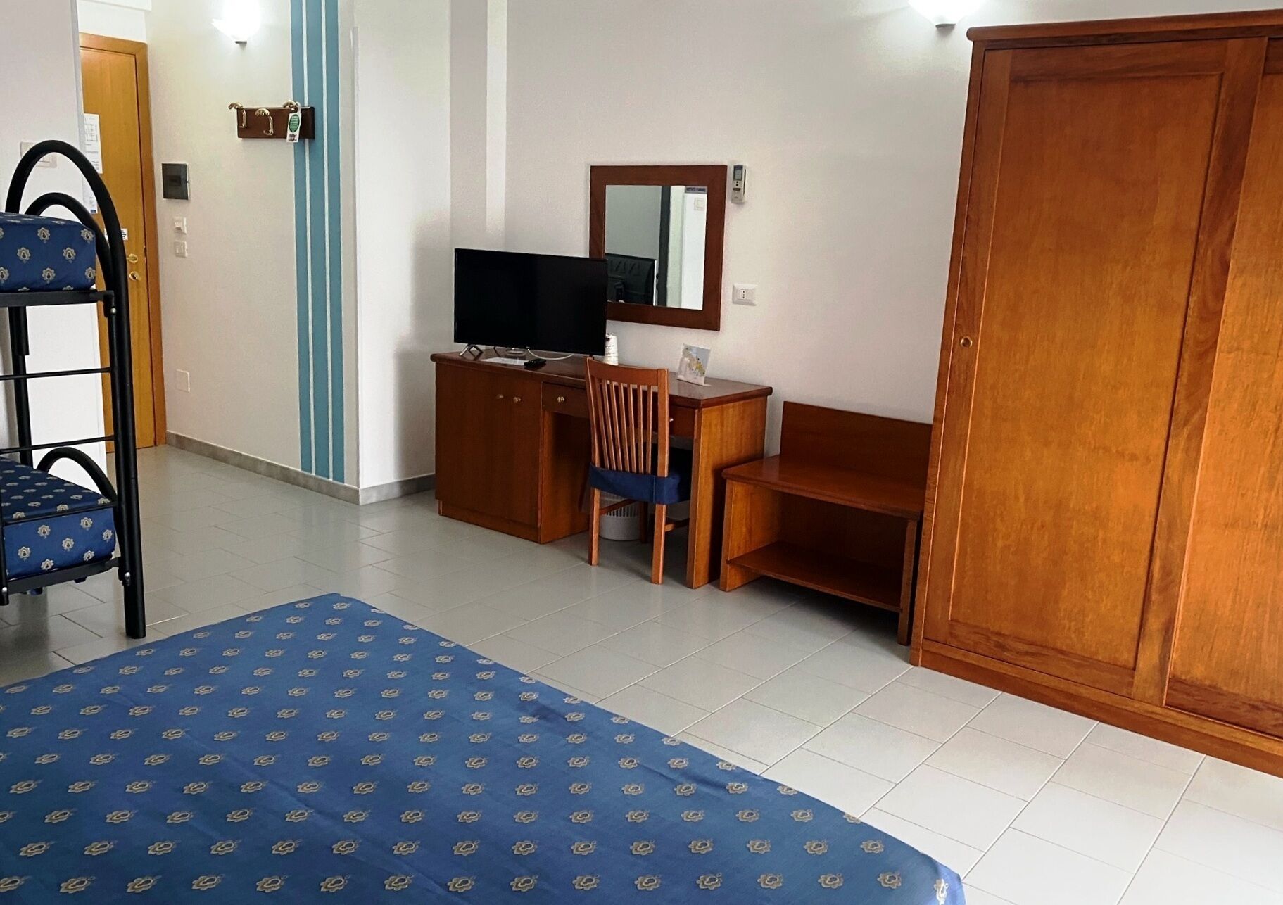 Quarto com cama, escrivaninha, cadeira, guarda-roupa e televisão.