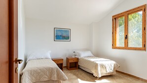 Quarto com duas camas, mesa de cabeceira, um quadro e uma janela.