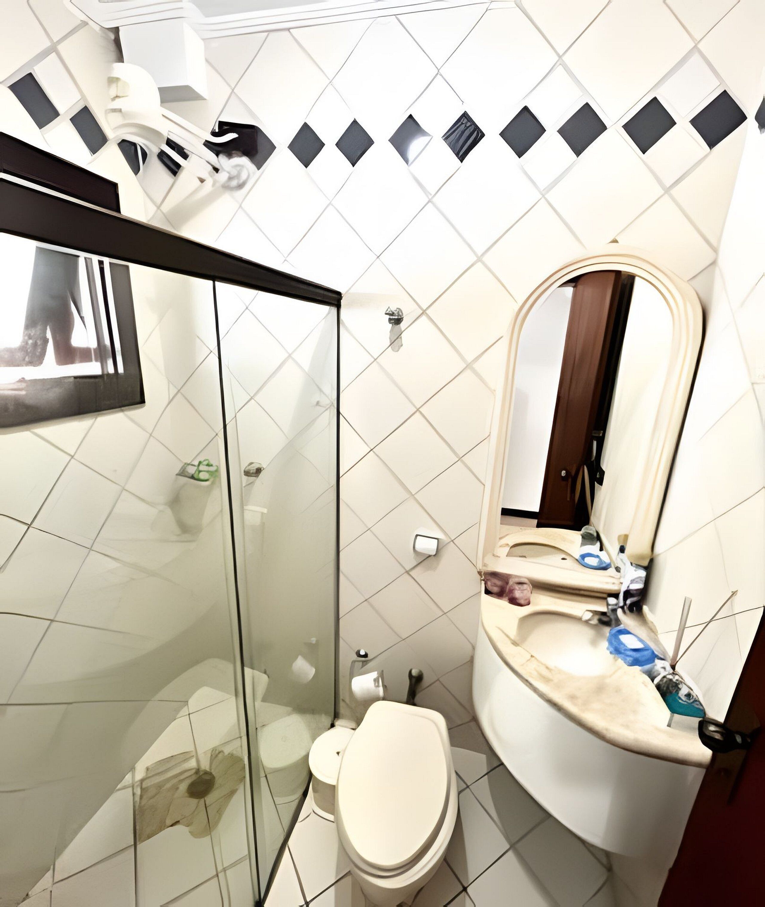 Um banheiro com box de vidro, vaso sanitário, pia com espelho e piso revestido de azulejos.