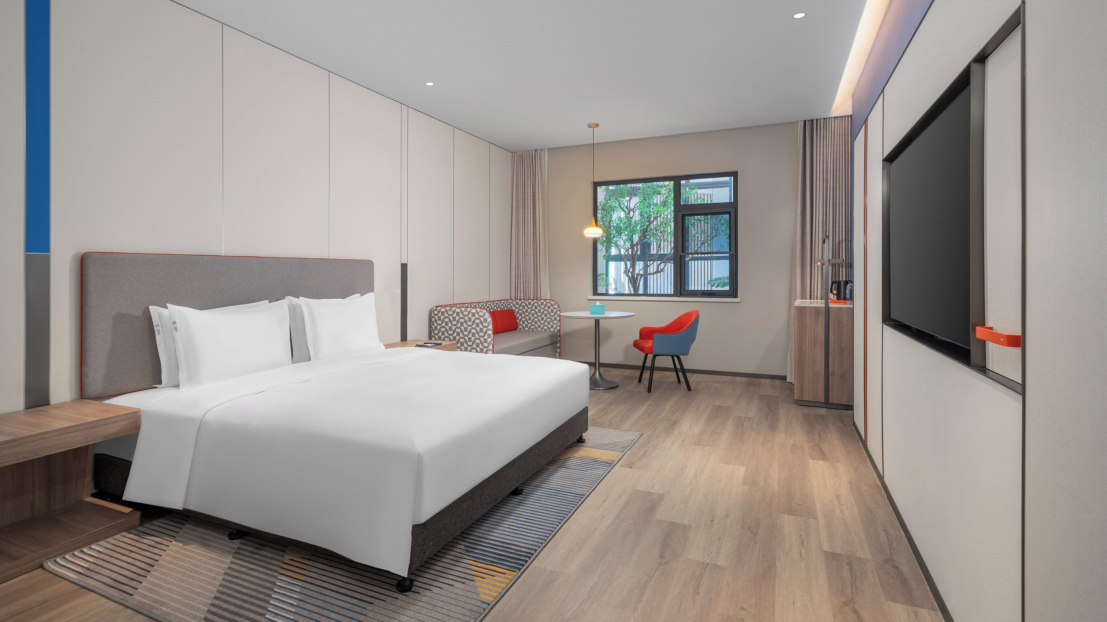 Quarto de hotel com cama, área de estar, pequena mesa, televisão e janela com vista.