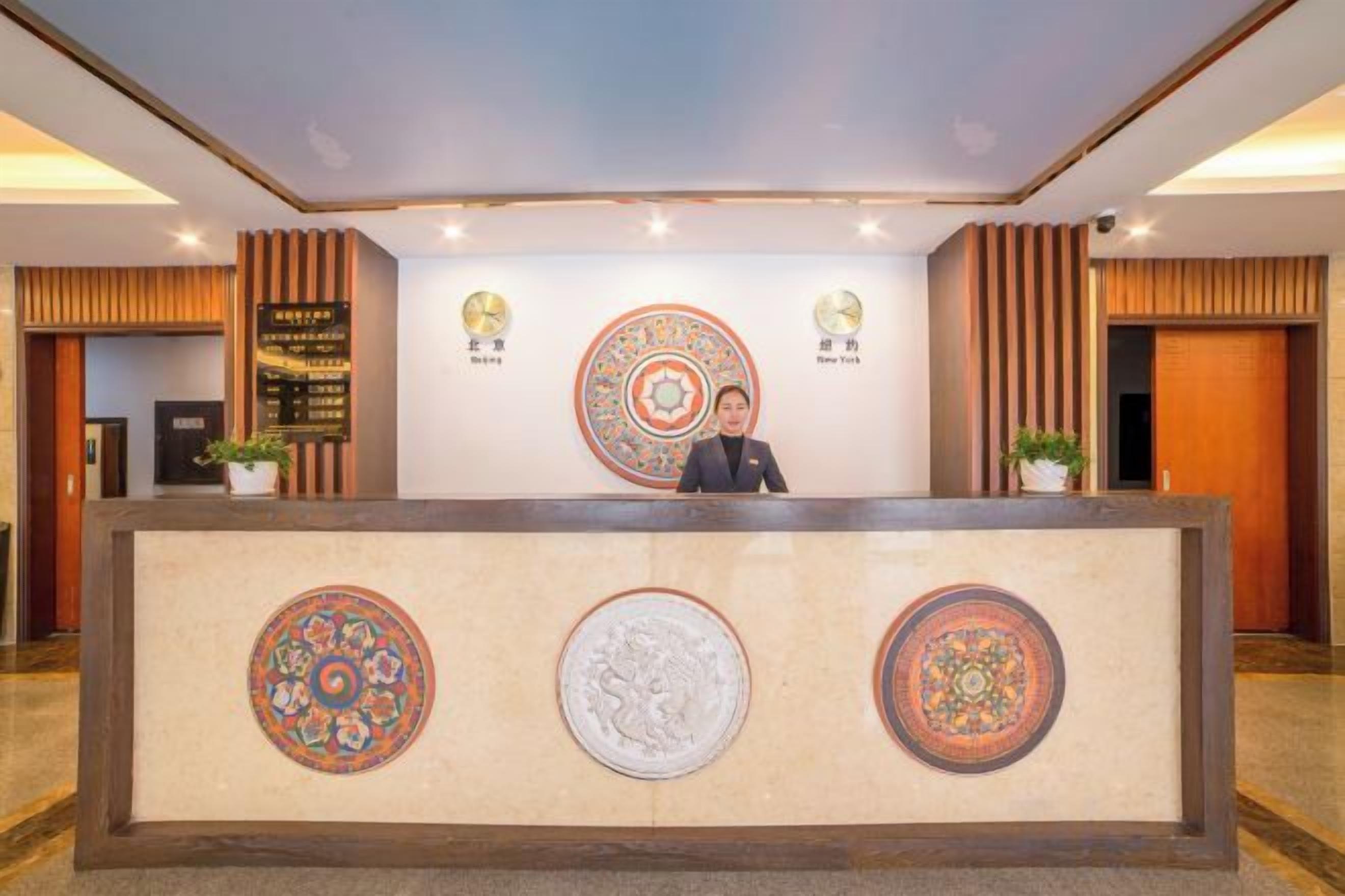 Bancada de recepção com recepcionista, painéis decorativos na parede e uma planta.