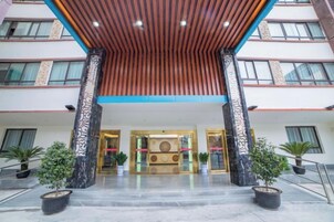 Entrada de hotel com teto de madeira, balcão de recepção e plantas em vasos.