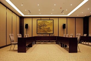 Uma sala de conferências com uma mesa comprida, cadeiras, piso coberto por carpete e um quadro na parede.