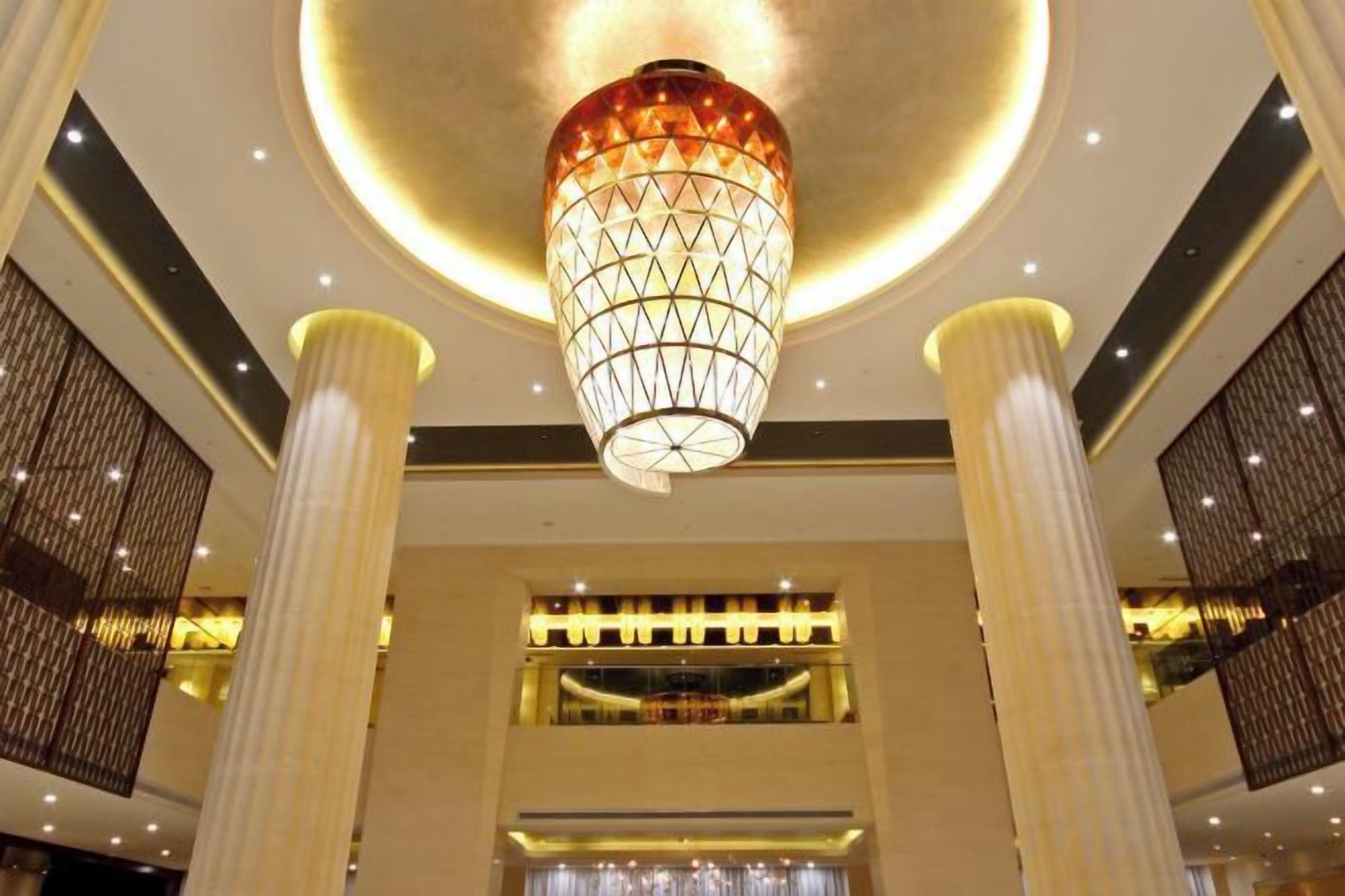 Um hall de entrada com um lustre grande e ricamente decorado, colunas altas e teto alto.