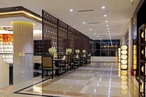Um saguão de hotel com piso xadrez, área de estar, parede decorativa e balcão de recepção.
