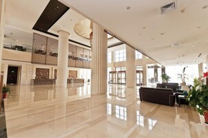 Um hall amplo com teto alto, janelas grandes e um balcão de recepção.