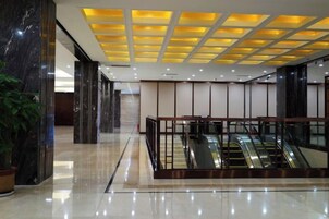 Um lobby moderno com elevador de vidro, piso de mármore e teto com iluminação embutida.