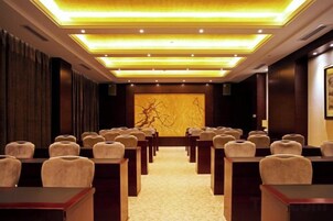 Uma sala de conferências com fileiras de cadeiras e mesas, uma tela grande na frente e um design moderno no teto.