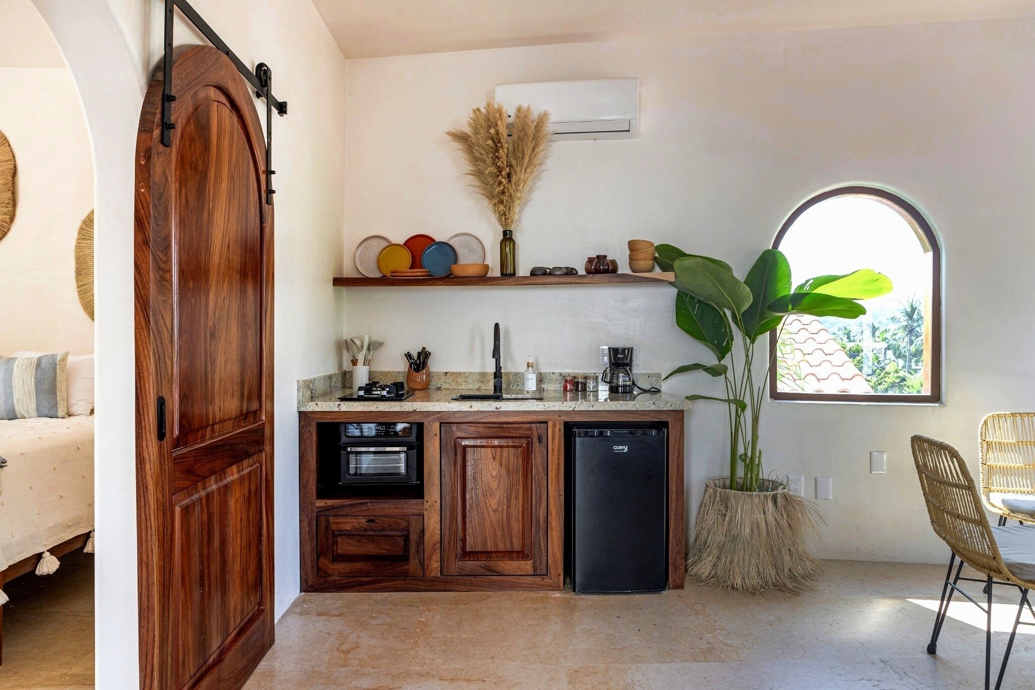 Cozinha com armários de madeira, lava-louças preta e máquina de café. Há uma janela com vista para vegetação lá fora.