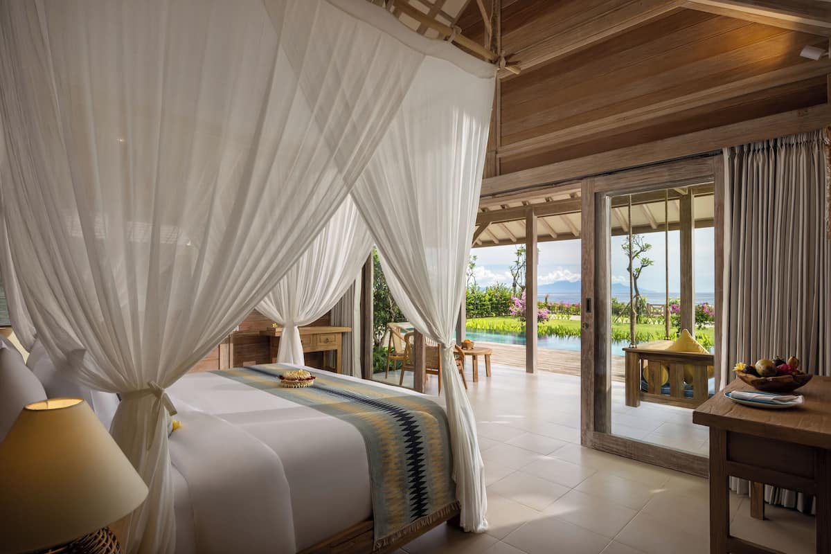 Um quarto espaçoso com uma cama grande, um dossel e vista para um jardim exuberante e piscina.