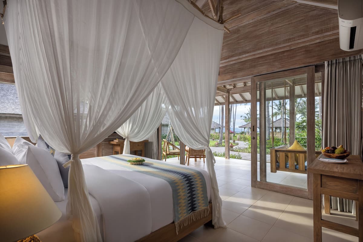 Quarto com cama de dossel, vista para o jardim e mesa de madeira com frutas.