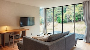 Uma sala de estar moderna com um sofá cinza, escrivaninha de madeira e televisão fixada na parede.