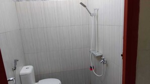 Casa de banho pequena com azulejos, vaso sanitário, chuveiro e um contentor de lixo preto.