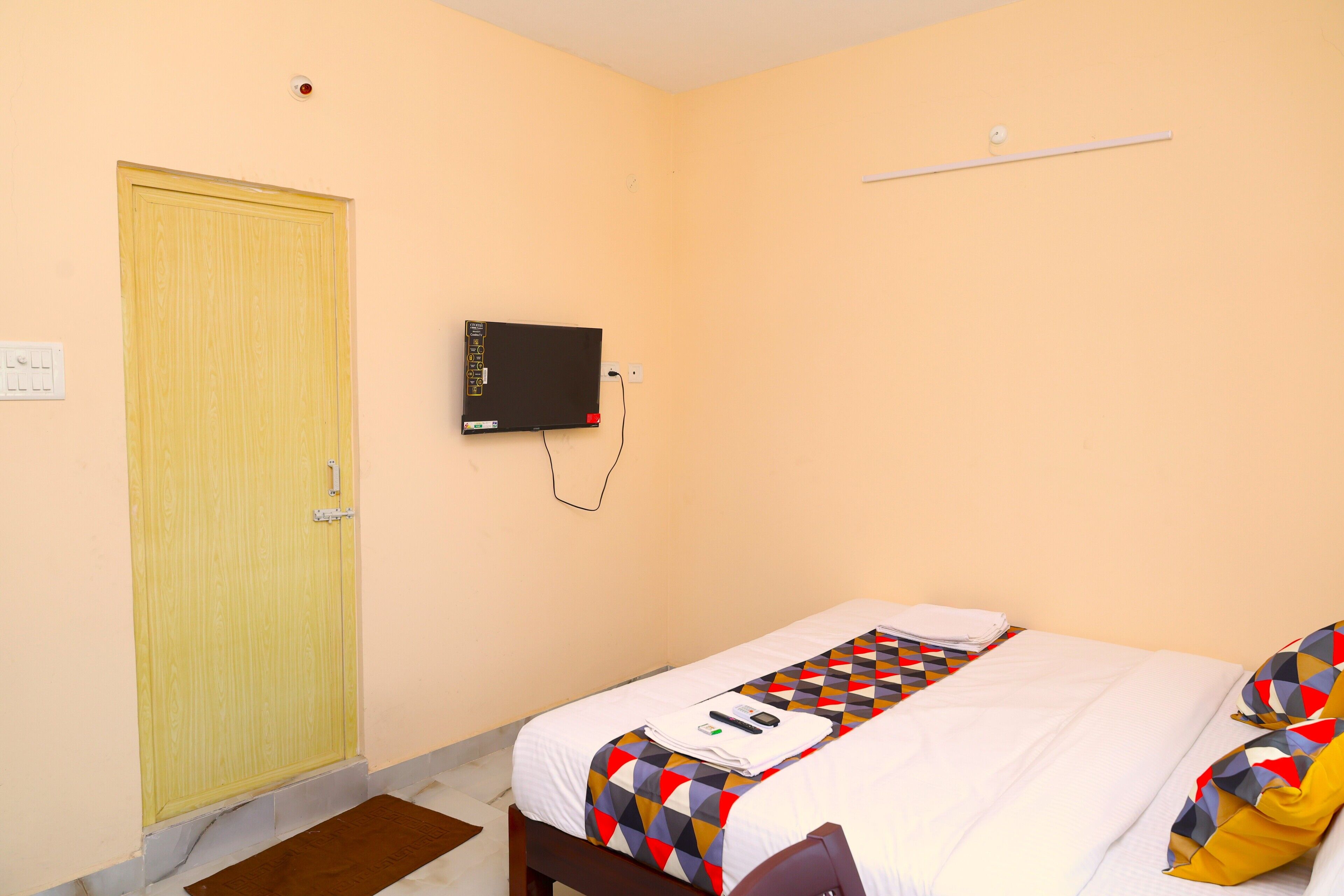 Quarto com cama, televisão fixada na parede e uma porta.