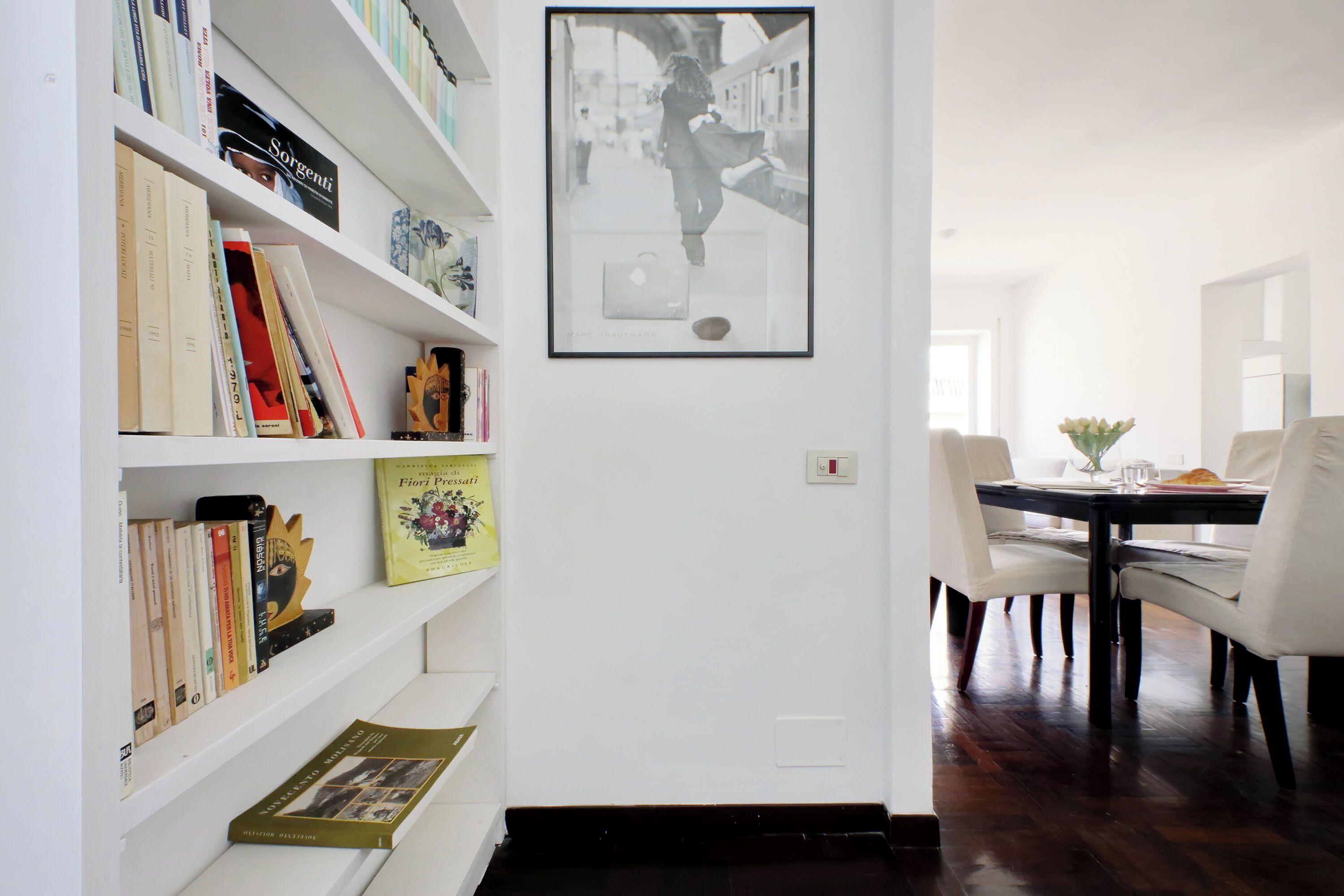 Uma estante bem organizada com vários livros e um quadro na parede.