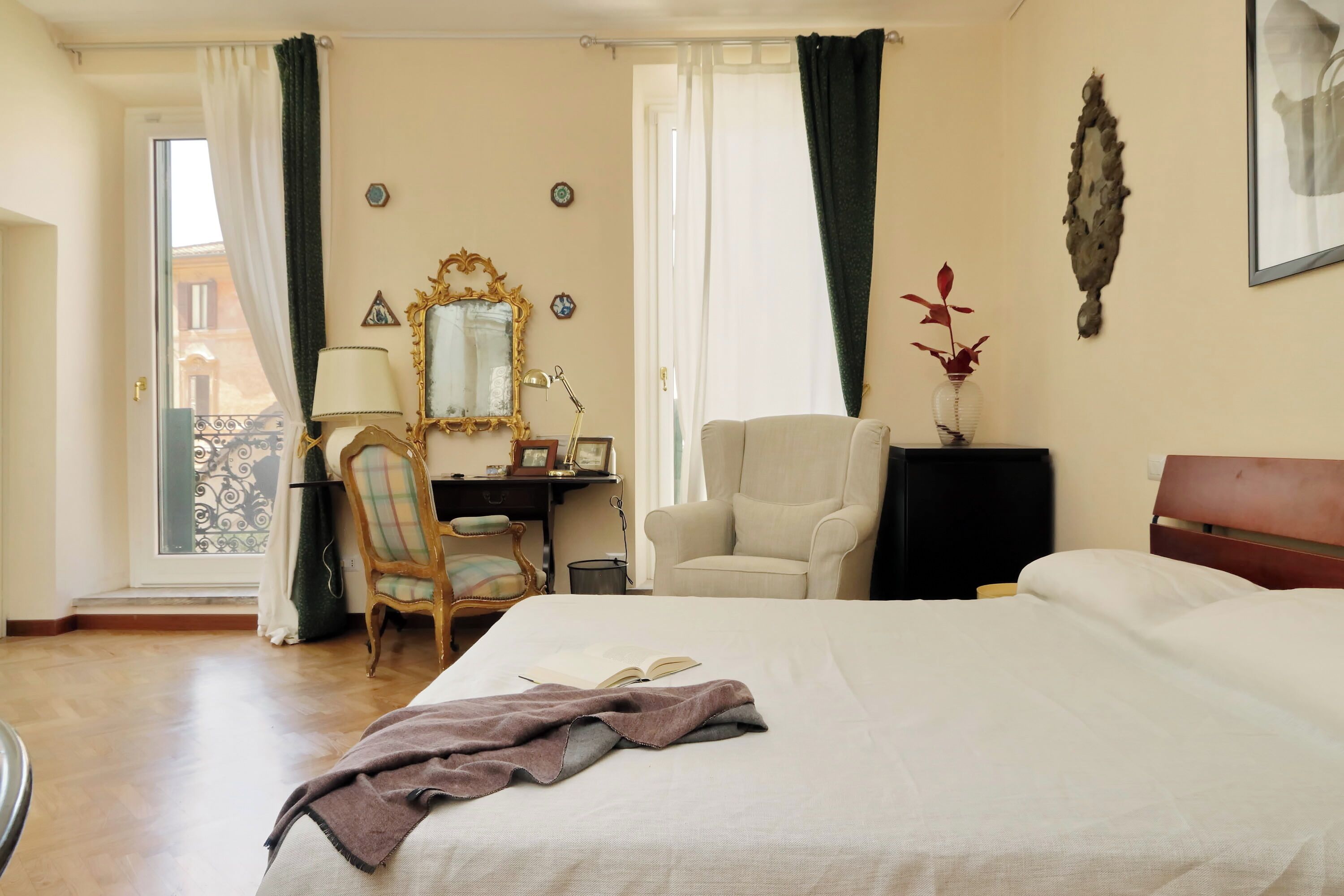 Quarto de hotel com cama, escrivaninha com luminária, cadeira, um espelho grande e vista para a varanda externa.
