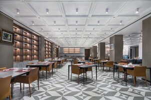 Um restaurante moderno com piso de padrão geométrico, várias mesas e cadeiras, e teto com iluminação embutida.