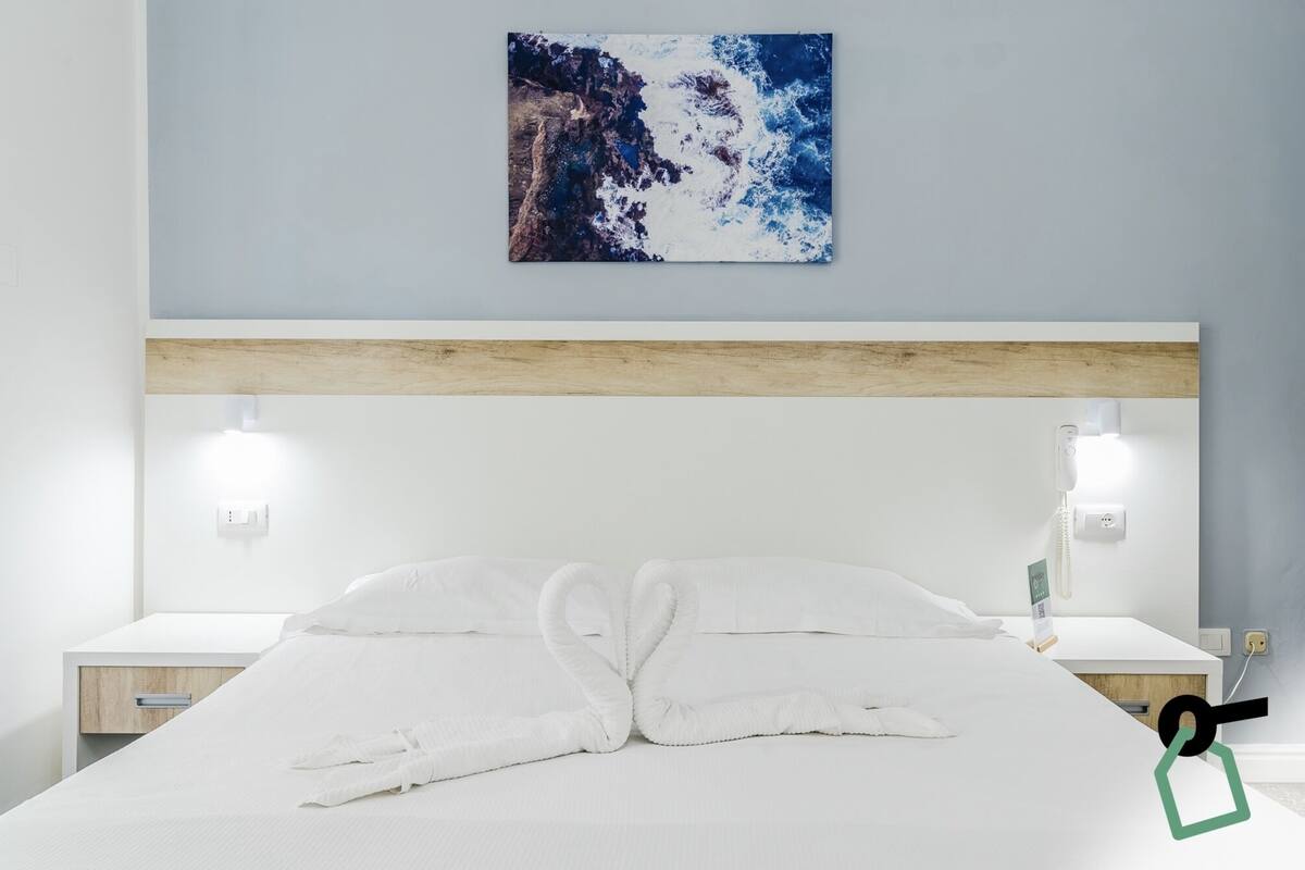 Quarto de hotel com uma cama, duas mesas de cabeceira, cabeceira de madeira e uma obra de arte na parede.