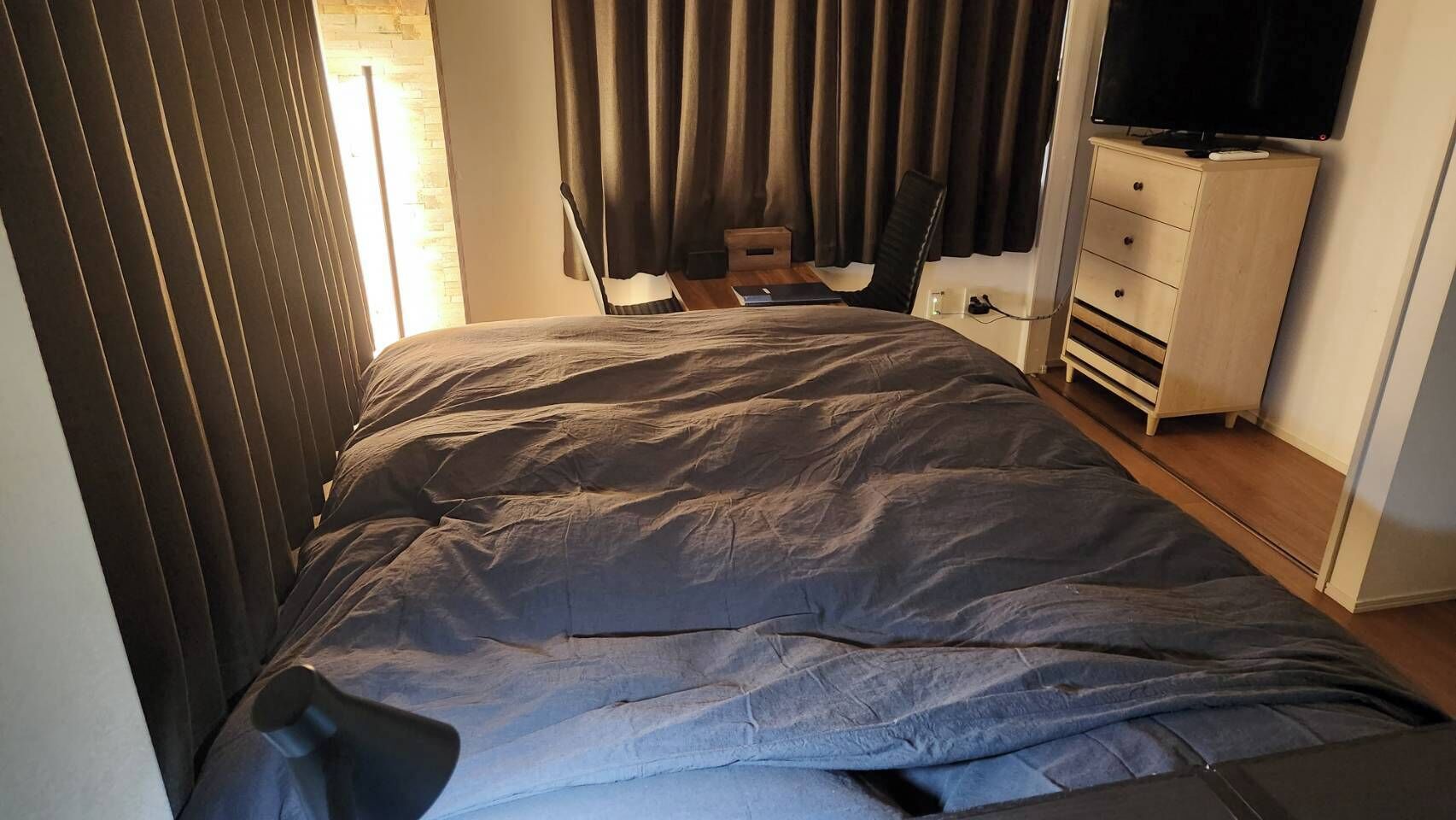 Quarto com uma cama, televisão, penteadeira e janela com cortinas.