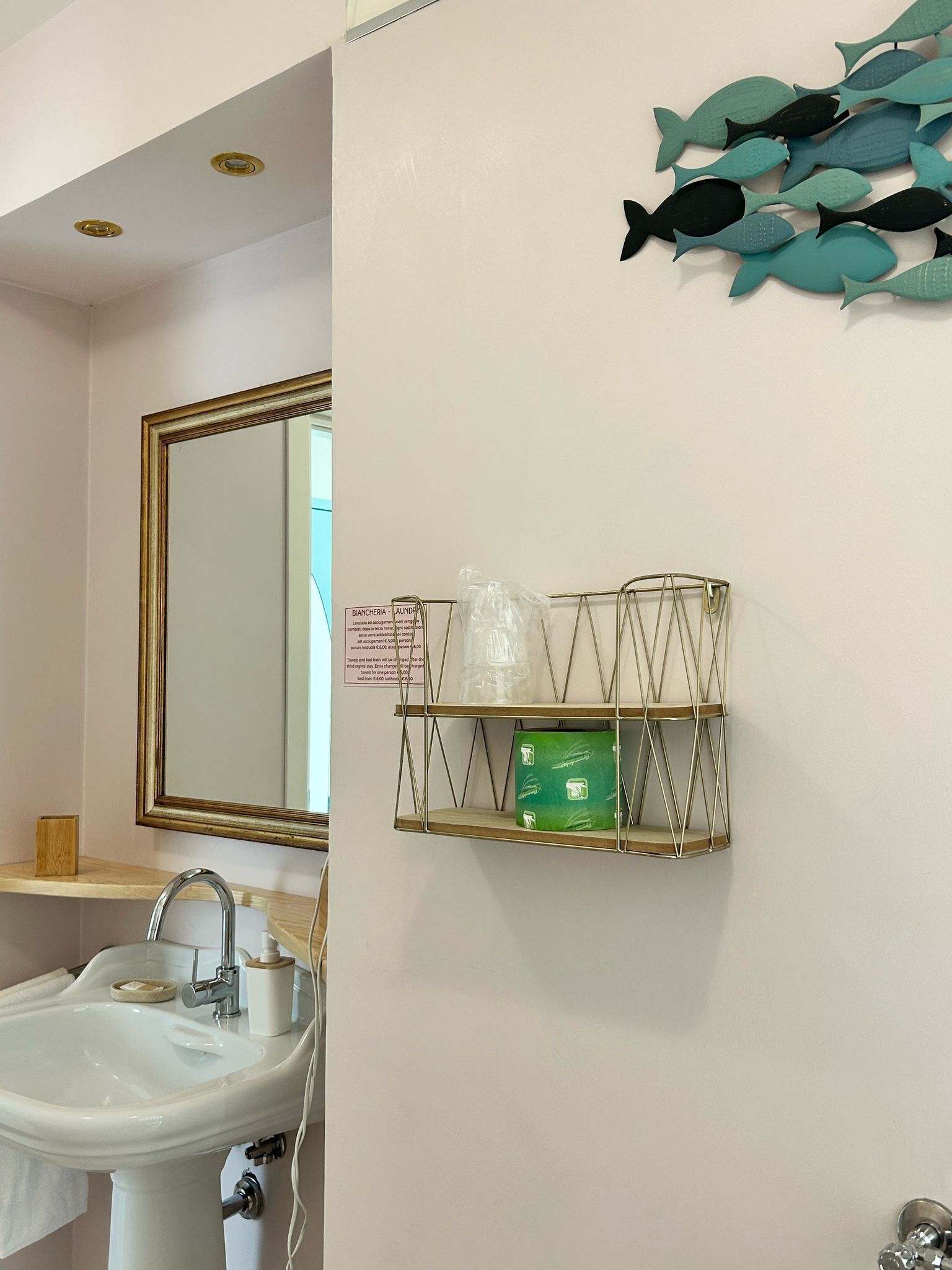 Casa de banho com uma pia branca, um espelho e uma prateleira na parede com produtos de higiene pessoal.
