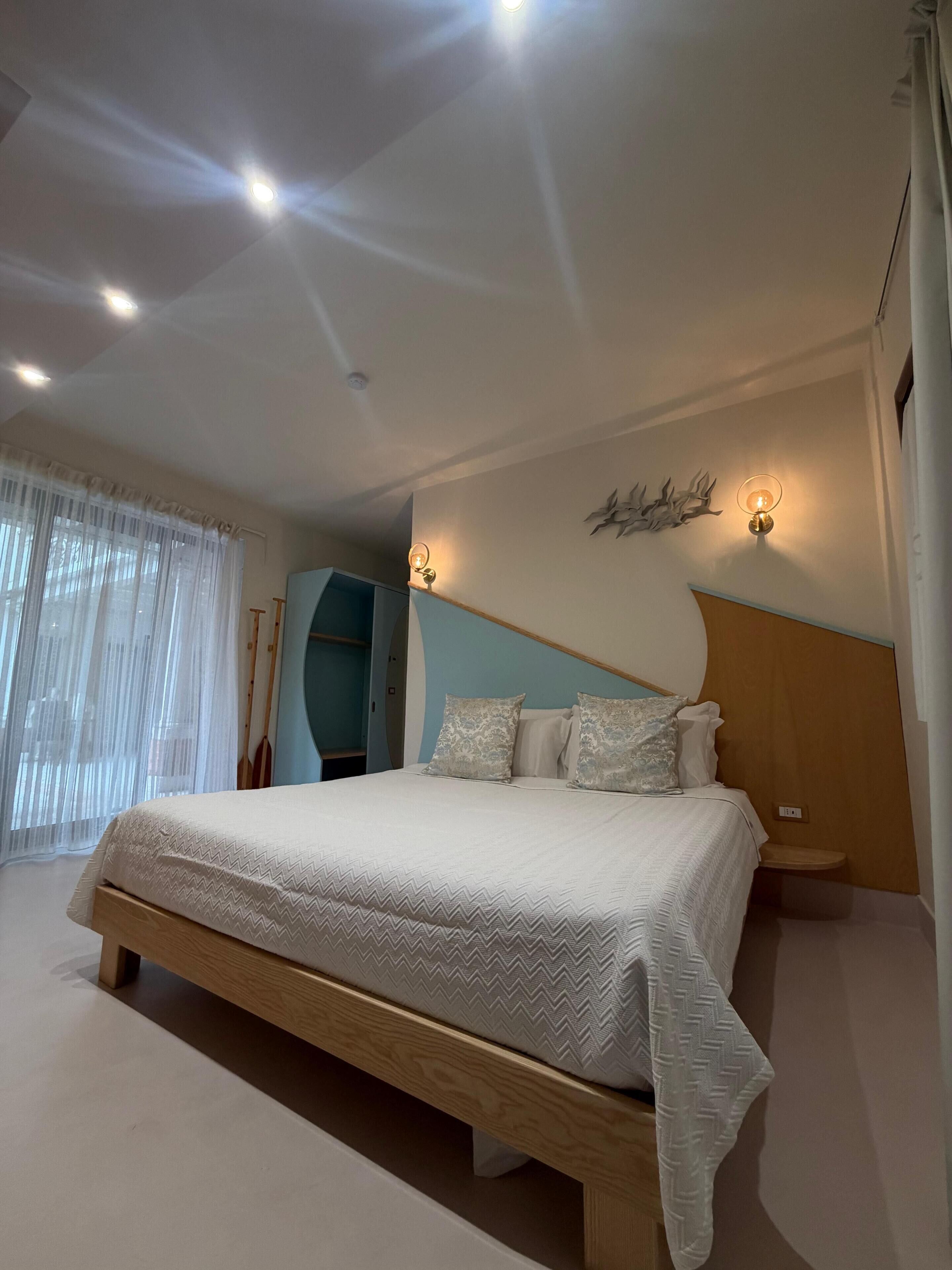 Quarto com uma cama grande, cabeceira de madeira e luminária fixada na parede.