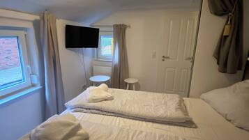 Quarto de hotel com duas camas, televisão fixada na parede, janela com cortinas e porta com uma toalha pendurada.