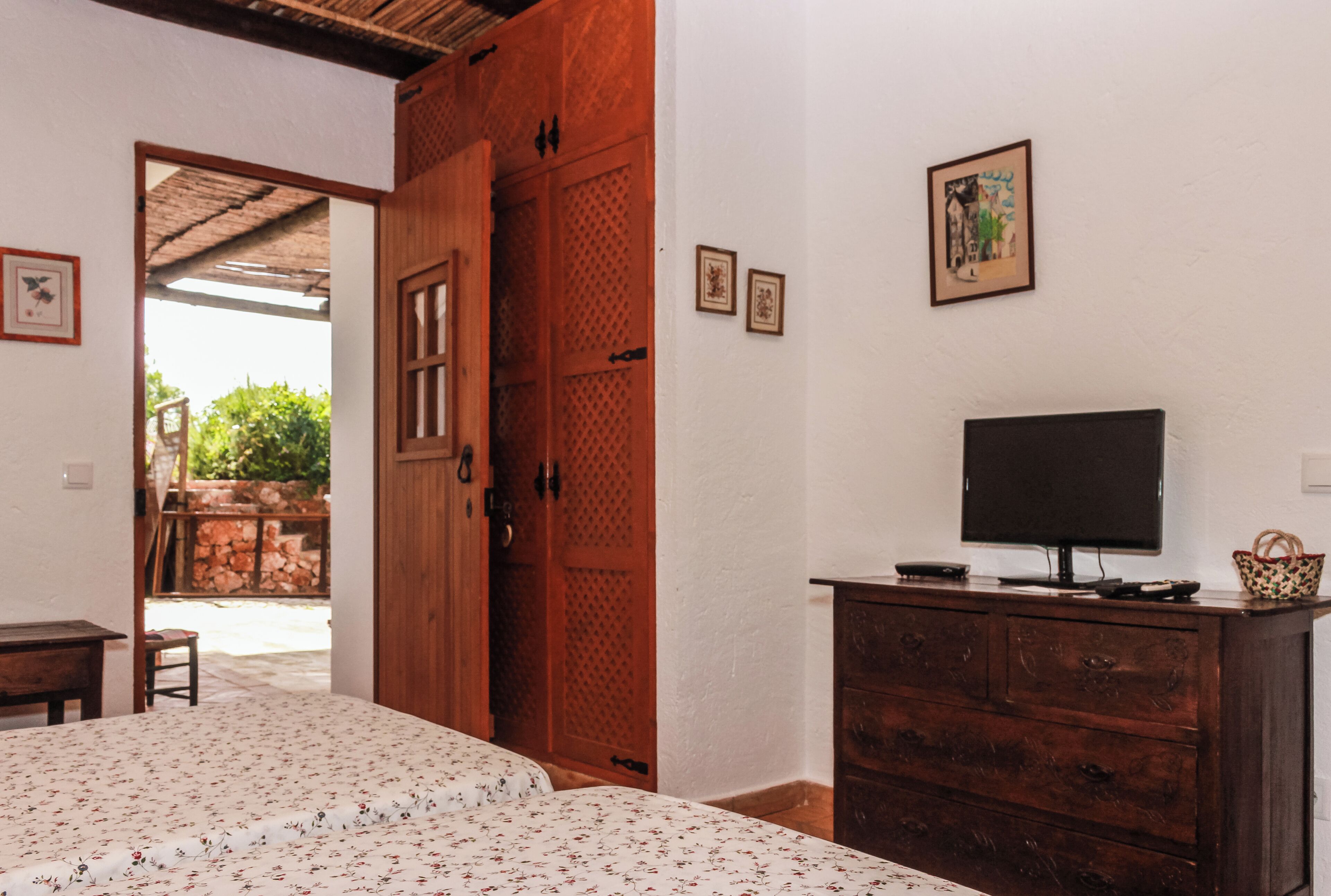 Quarto com cama, guarda-roupa de madeira, televisão e quadros nas paredes.