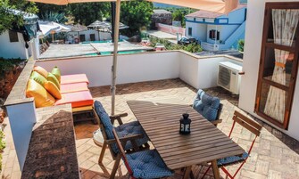 Um pátio com mesa e cadeiras de madeira, um banco estofado e uma piscina ao fundo.