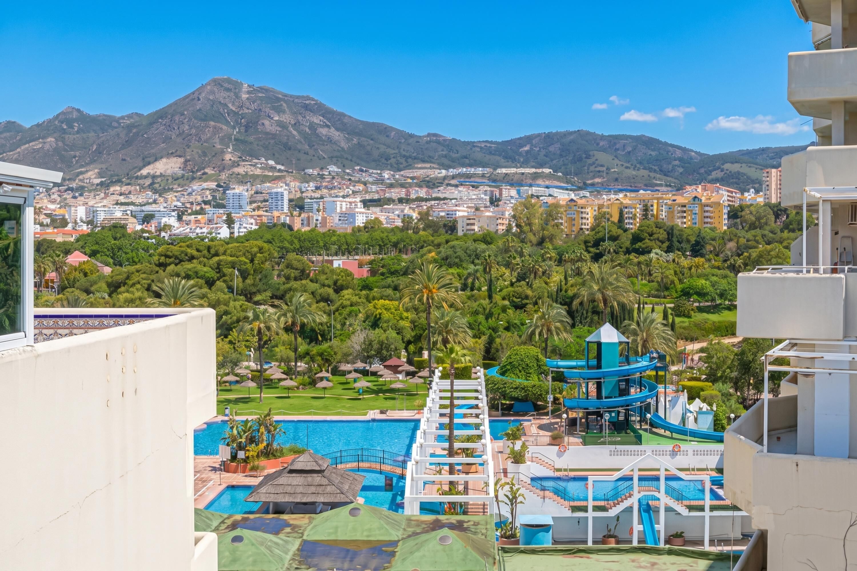 Resort com piscina, escorrega aquático e vista para uma cidade e montanhas ao fundo.