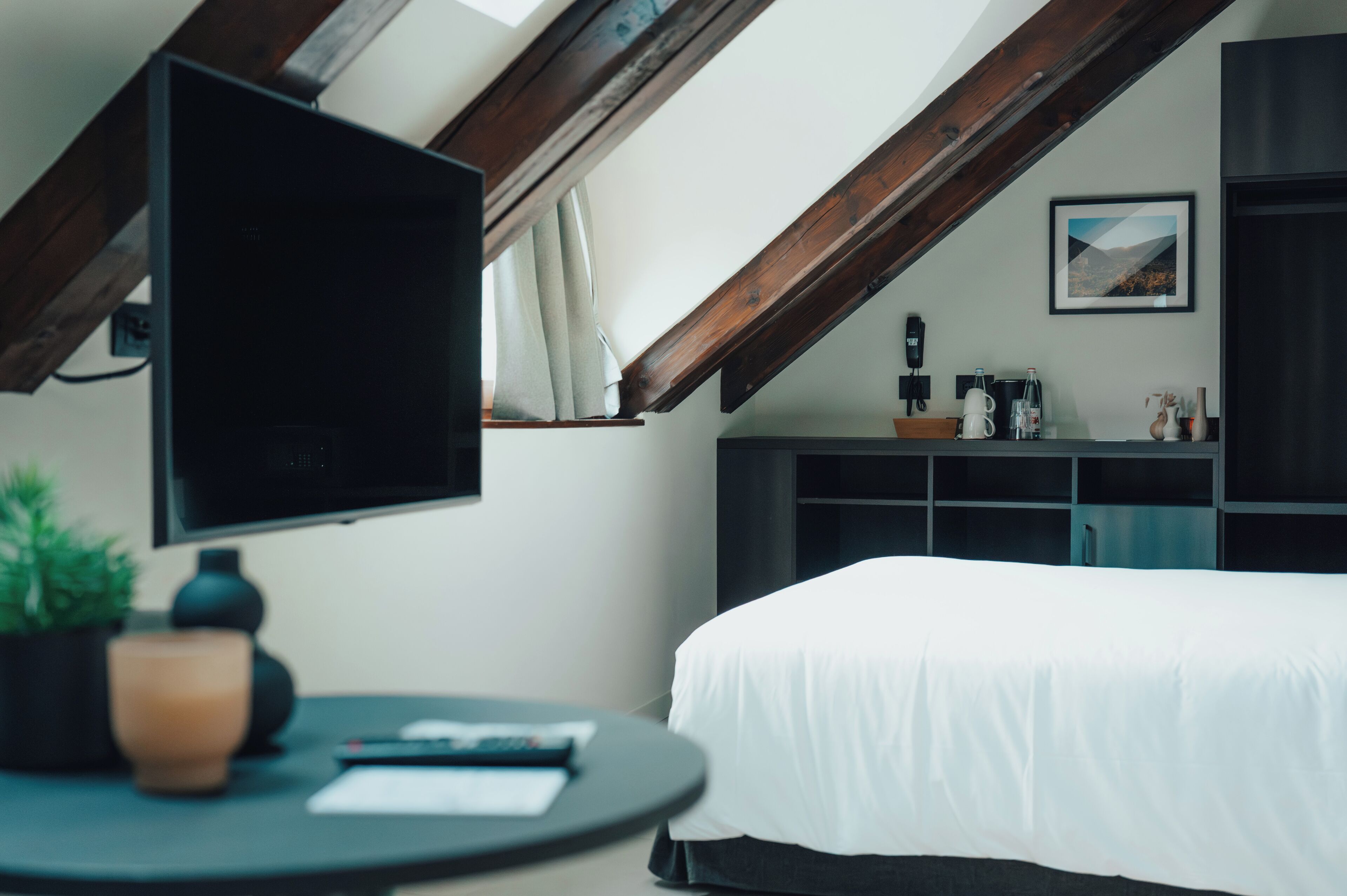 Quarto com cama, escrivaninha, cadeira, televisão e janela.