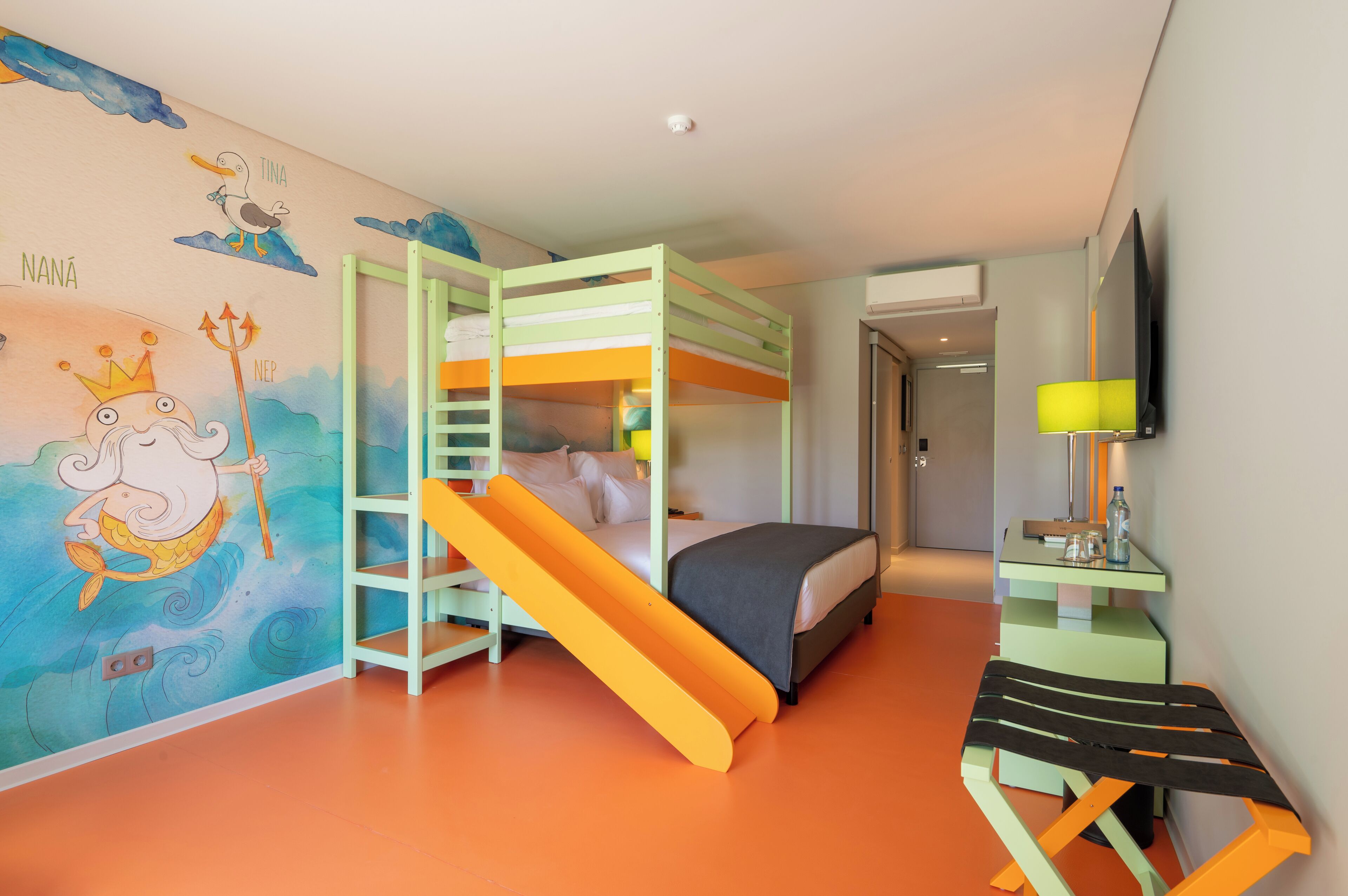 Quarto infantil com beliches, um escorrega e um mural na parede.
