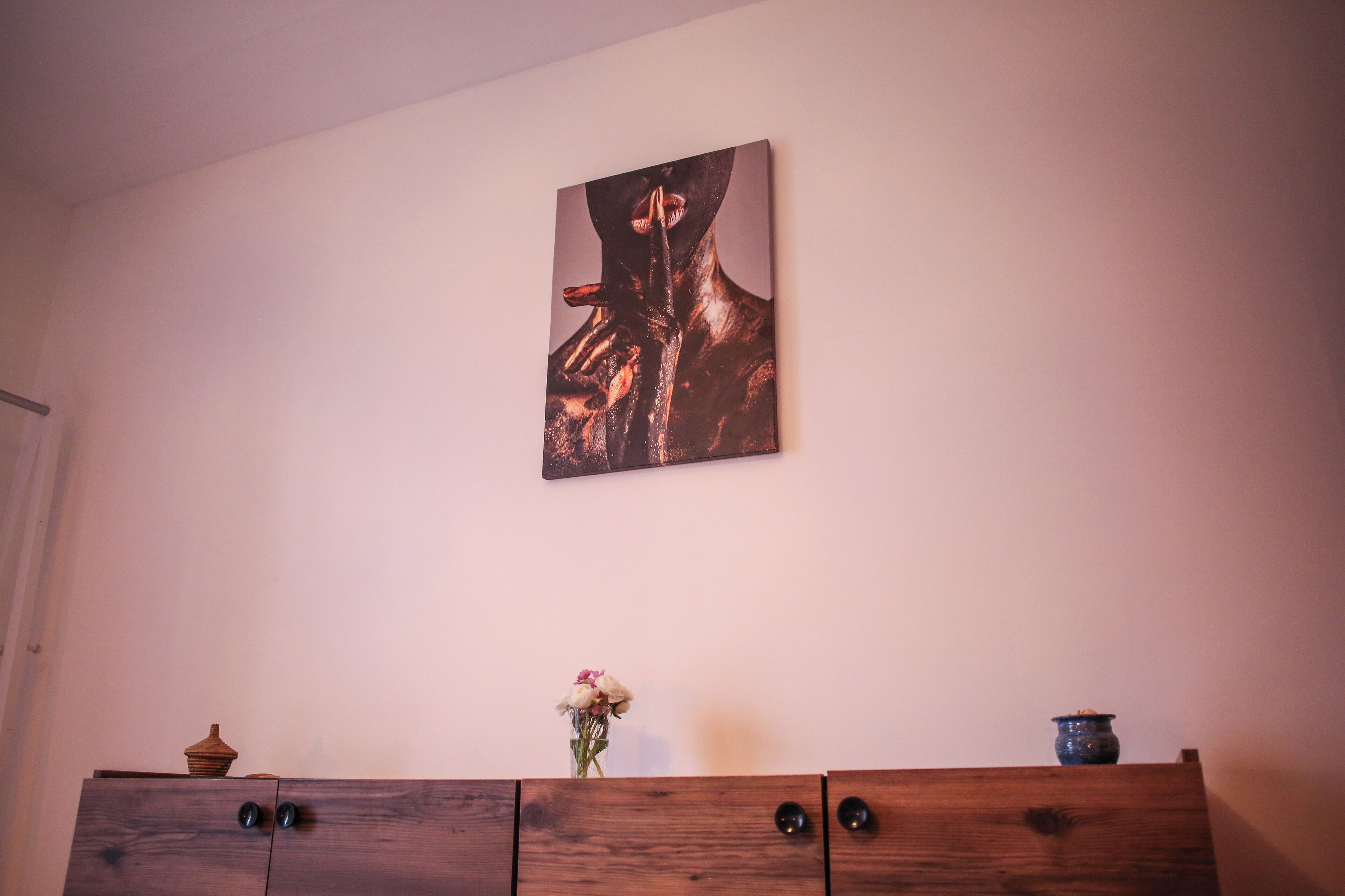 Um armário de madeira com um vaso de flores e um quadro na parede.