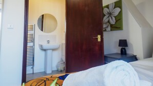 Quarto de hotel com uma cama, banheiro com pia e espelho, e um quadro na parede.