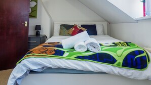 Uma cama bem arrumada com um edredom colorido, um travesseiro estampado com flores e uma toalha enrolada sobre a cama.