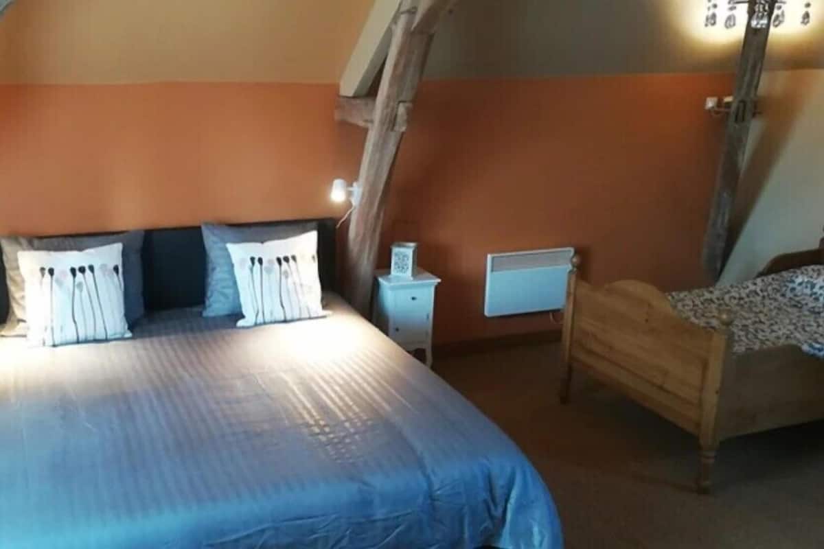 Quarto com cama, mesas de cabeceira, uma cadeira de madeira e teto inclinado.