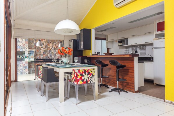Uma sala de jantar com mesa e cadeiras, uma cozinha com armários brancos e uma parede amarela de destaque.