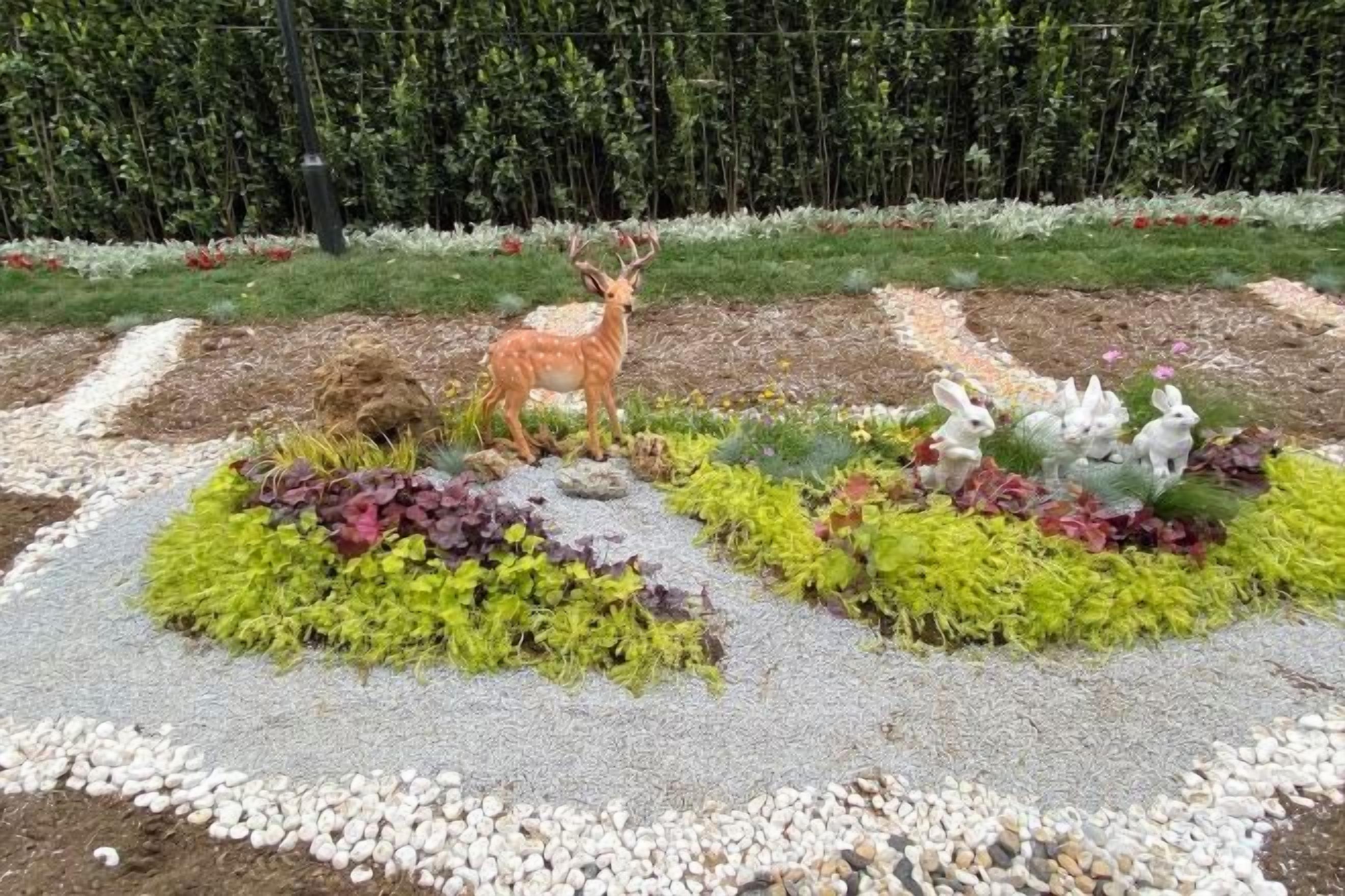 Jardim com estátua de veado, diversas plantas e um sebe ao fundo.