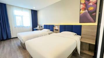 Quarto de hotel com duas camas, uma escrivaninha, uma cadeira e uma janela grande com cortinas.