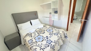 Um quarto com cama, mesa de cabeceira, guarda-roupa e espelho.