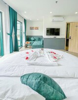 Quarto de hotel com uma cama grande, cortinas verde-água, um sofá, uma televisão e um aparelho de ar condicionado.