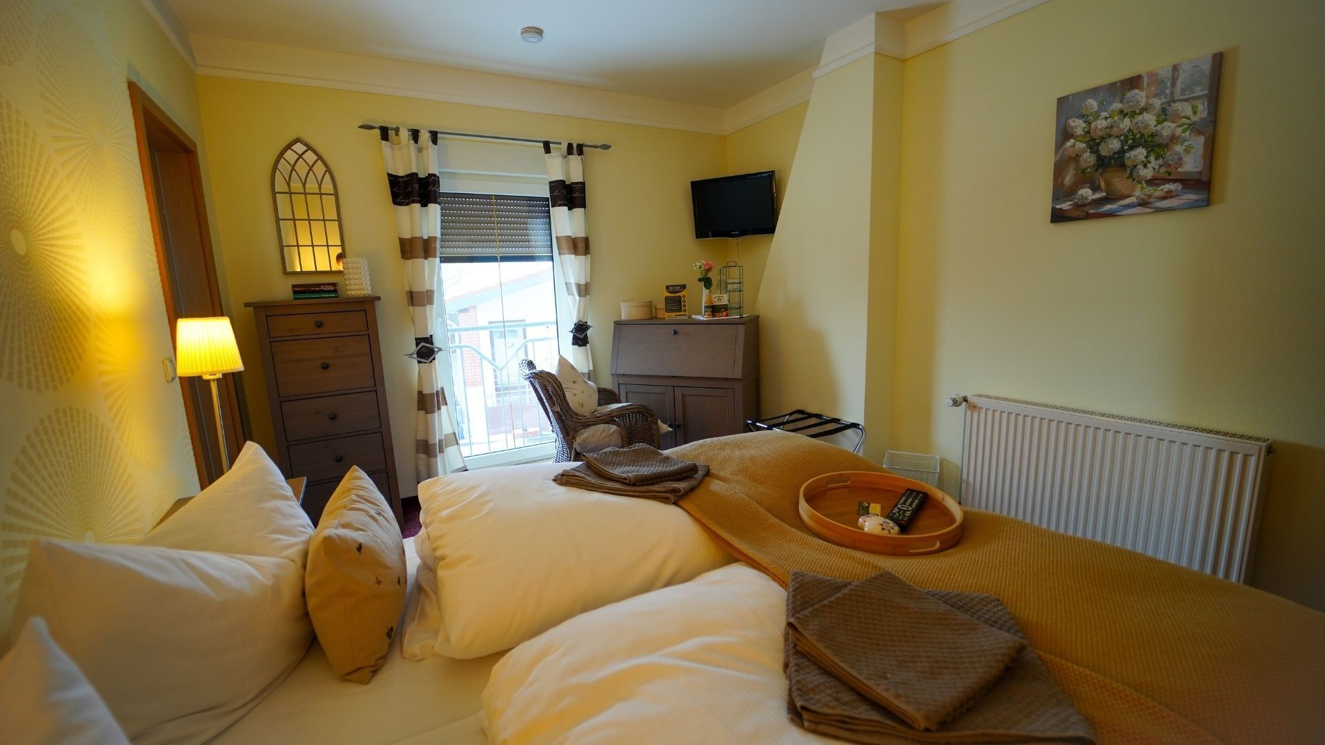 Quarto de hotel com cama, escrivaninha, cadeira, cômoda, televisão e janela com cortinas.