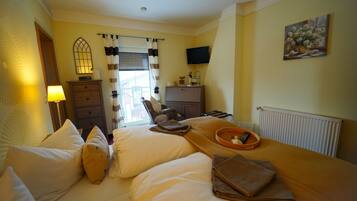 Quarto de hotel com cama, escrivaninha, cadeira, cômoda, televisão e janela com cortinas.