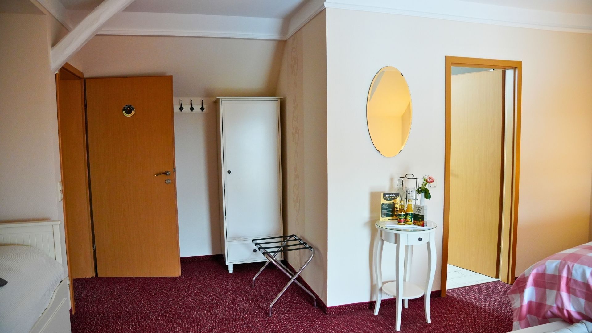 Quarto de hotel com porta de madeira, guarda-roupa branco, pequena mesa com espelho e tapete vermelho.